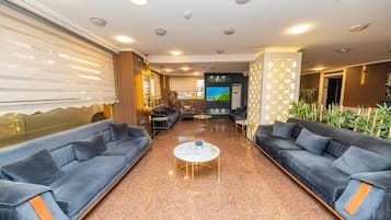 Um lobby de hotel moderno com dois sofás, uma mesa de centro e uma televisão.