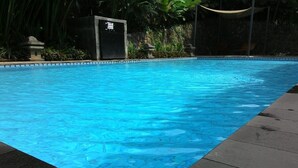 Piscina com água azul cristalina, rodeada por um deck de pedra e vegetação.