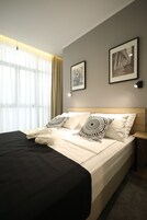Cama bem arrumada com lençóis brancos e almofadas estampadas, cabeceira de madeira e duas fotos emolduradas na parede.