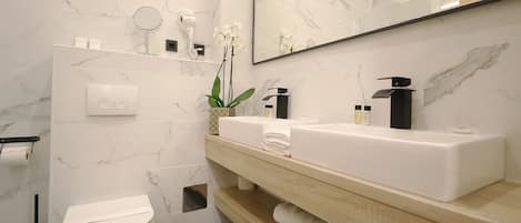 Uma casa de banho moderna com sanita branca, um espelho grande, lavatório branco e parede de mármore.