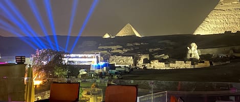 Vista das pirâmides à noite, com um palco e cadeiras em primeiro plano.
