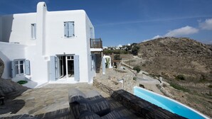Um edifício branco com piscina e escadaria de pedra, e vista para uma encosta rochosa.