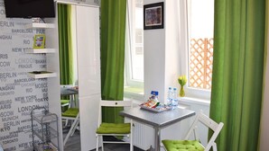 Quarto com decoração em tons de verde, incluindo cortinas e almofadas verdes, uma mesinha com lanches e bebidas, e uma parede com nomes de cidades.