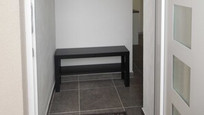 Um corredor estreito com um banco, um cabideiro e uma porta com painéis de vidro jateado.