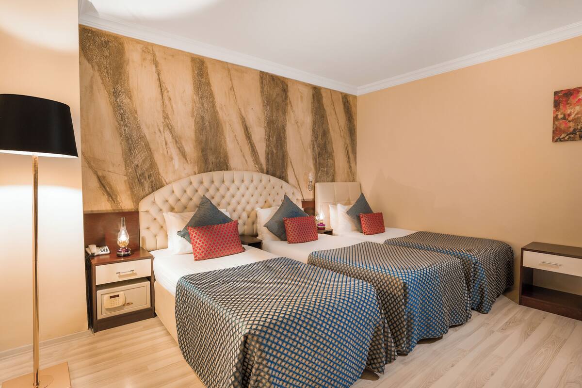 Quarto de hotel com duas camas, uma cabeceira grande com textura tufada, uma mesa de cabeceira com abajur e uma parede com padrão semelhante ao mármore.
