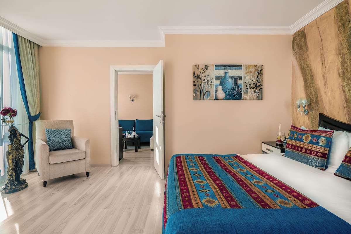 Quarto de hotel com uma cama, uma cadeira, uma escrivaninha e um quadro na parede.