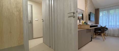 Quarto de hotel com porta deslizante, escrivaninha com cadeira, televisão na parede e janela com cortinas.