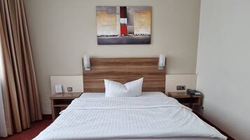 Quarto de hotel com uma cama grande, cabeceira de madeira, duas mesas de cabeceira com luminárias, um telefone e um quadro na parede.