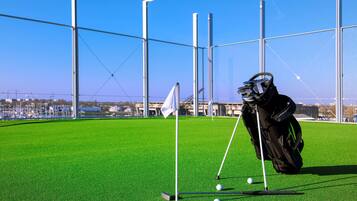 Uma área de treino de golfe com um campo verde, uma bolsa de golfe e um mastro com bandeira.