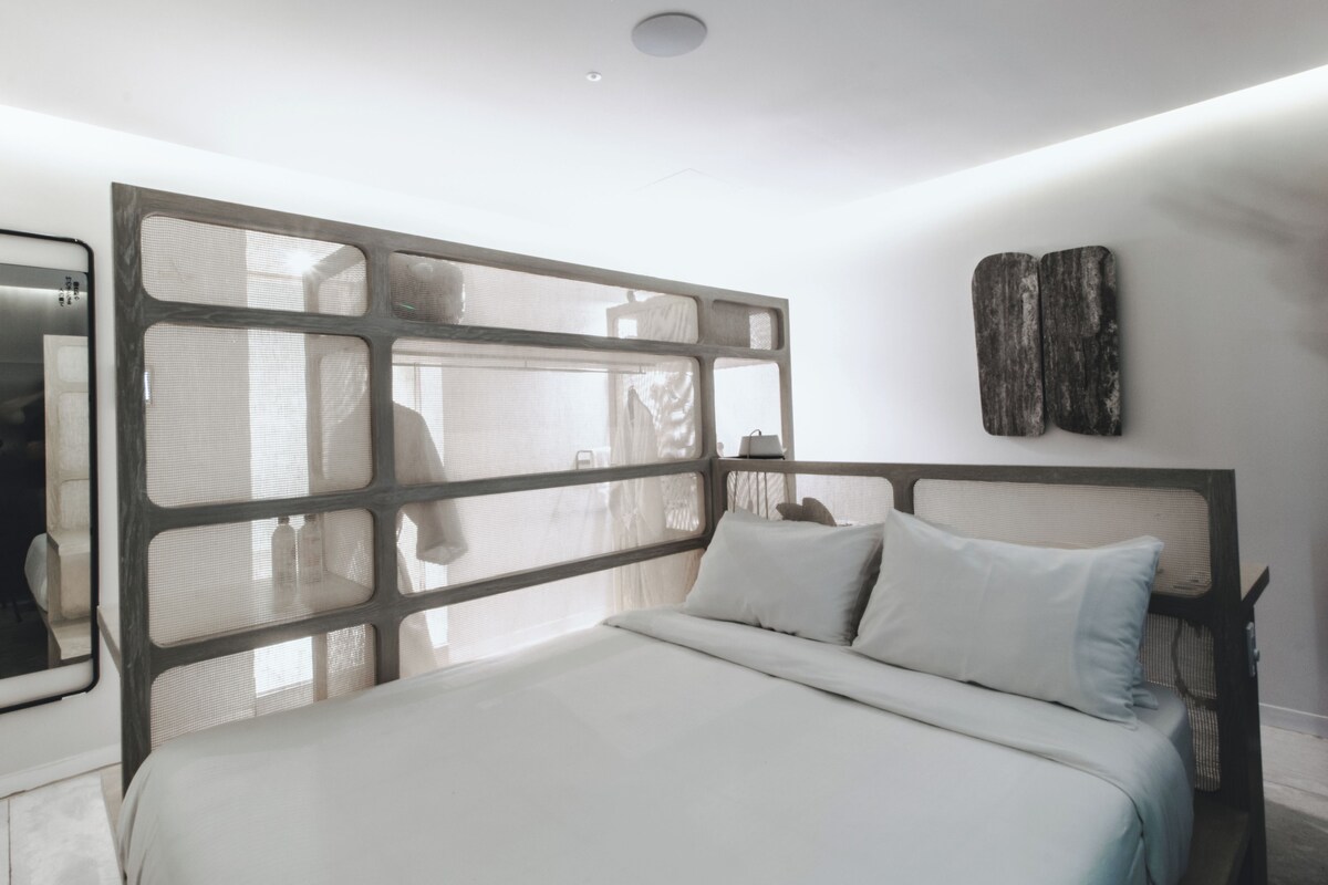 Um quarto moderno com uma cama grande, uma cabeceira com design geométrico e uma obra de arte na parede.