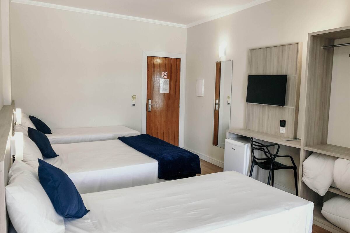 Quarto de hotel com duas camas de solteiro, uma escrivaninha com cadeira, televisão e um pequeno frigorífico.