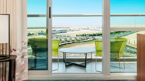 Varanda com mesa e cadeiras, com vista para uma área ajardinada e edifícios ao longe.