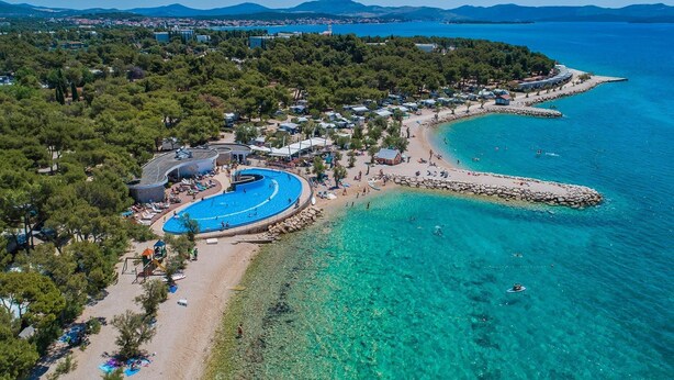 Vista aérea de um resort à beira-mar, com uma grande piscina, praia e águas azul-turquesa cristalinas.