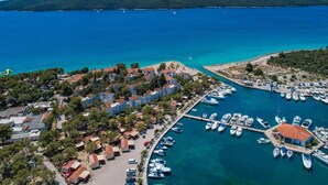 Vista aérea de uma vila costeira com um porto de recreio, casas com telhados vermelhos e barcos atracados.