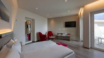 Quarto de hotel moderno com uma cama grande, uma TV fixada na parede e uma varanda com mesa e cadeiras.