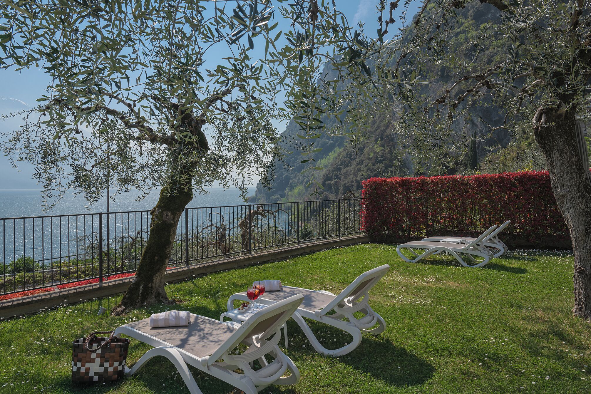 Um terraço com duas cadeiras de descanso brancas, uma mesa com uma bebida e vista para o mar e montanhas.
