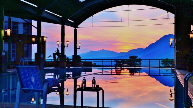 Terraço com vista para montanhas e piscina. Há cadeiras e uma mesa com garrafas.