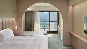 Quarto de hotel com uma cama grande, televisão, escrivaninha e varanda com vista para a cidade.