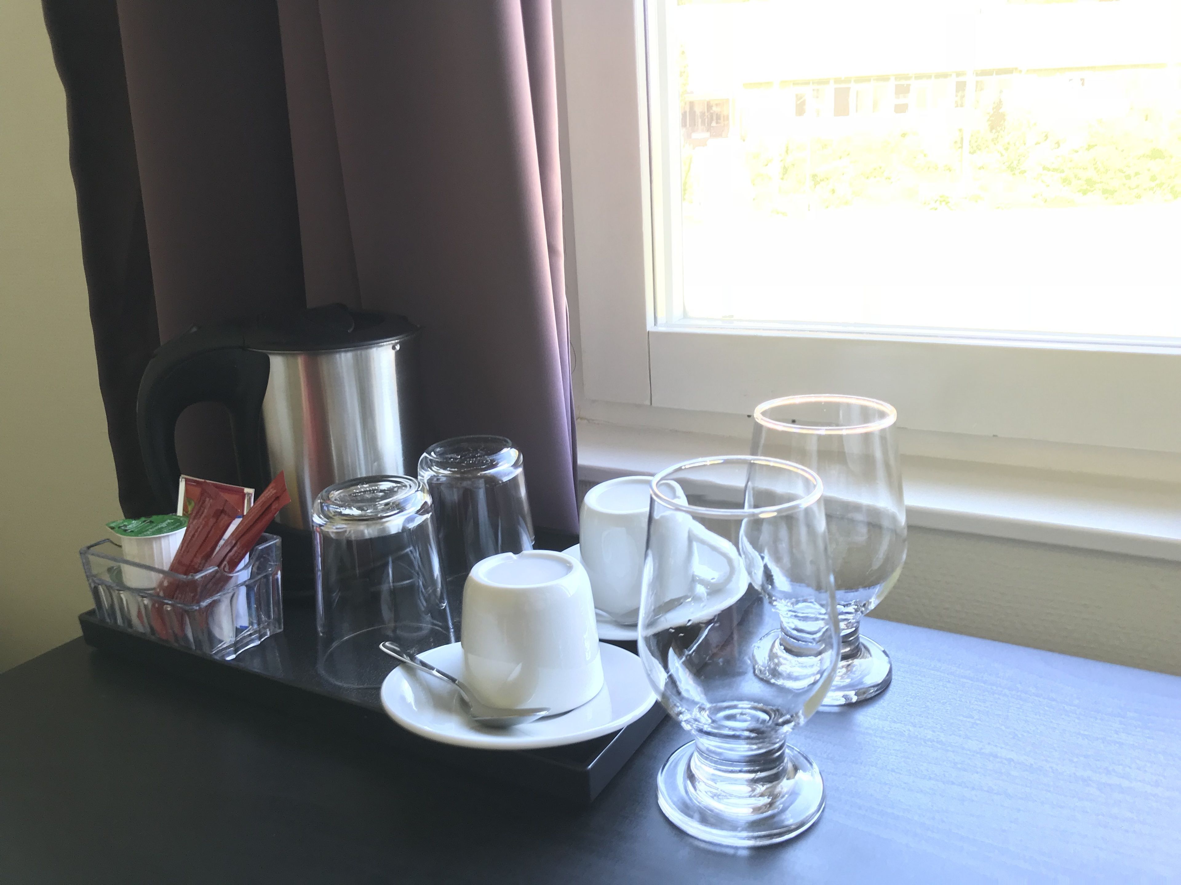 Uma mesa com uma cafeteira, copos e um recipiente de vidro com utensílios.