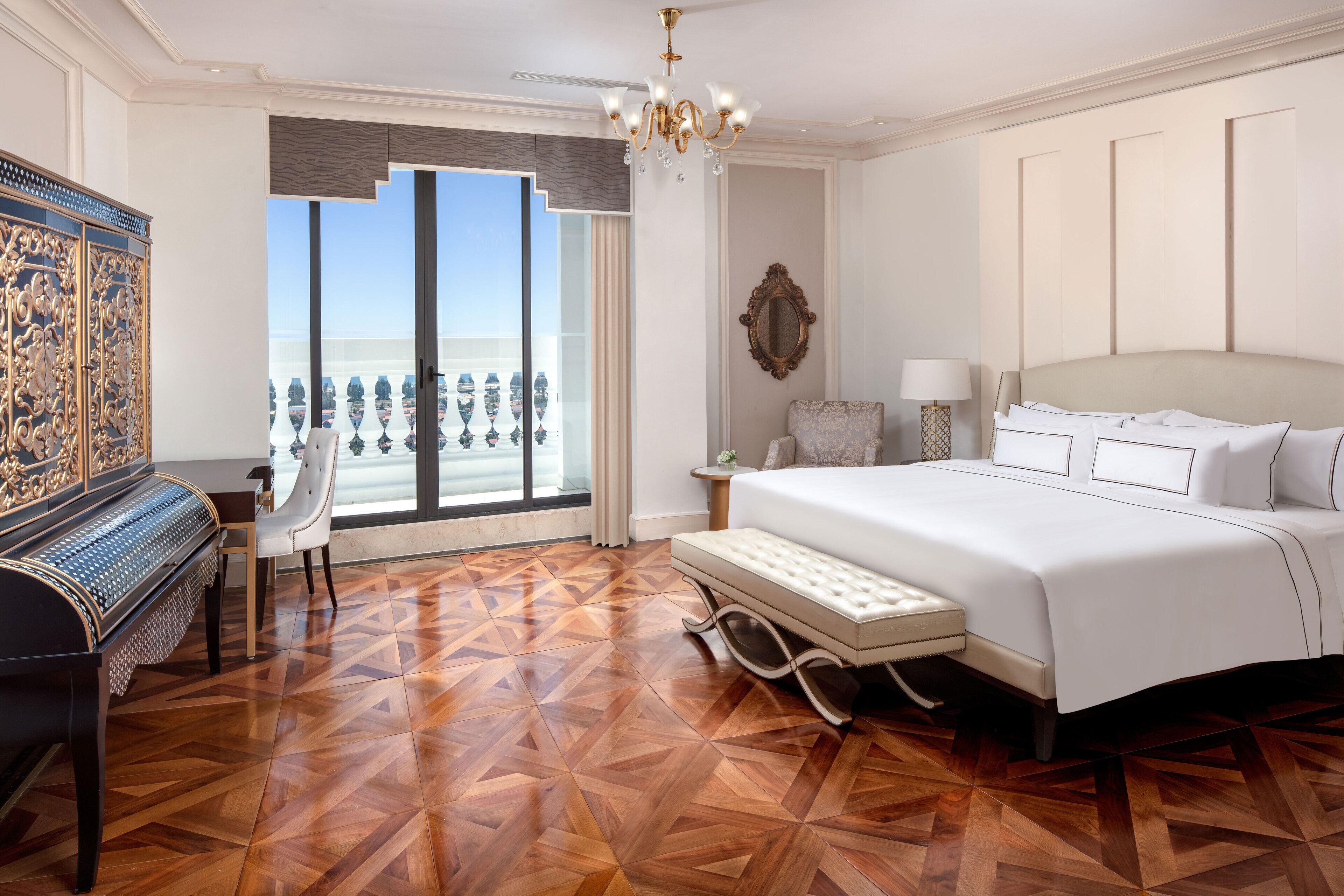 Quarto de hotel com uma cama grande, um piano, um banquinho e vista para o mar.
