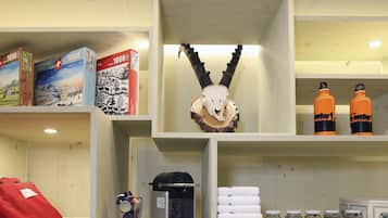 Uma estante com caixas de quebra-cabeça, uma decoração de caveira, garrafas de água, uma máquina de café, toalhas e potes.