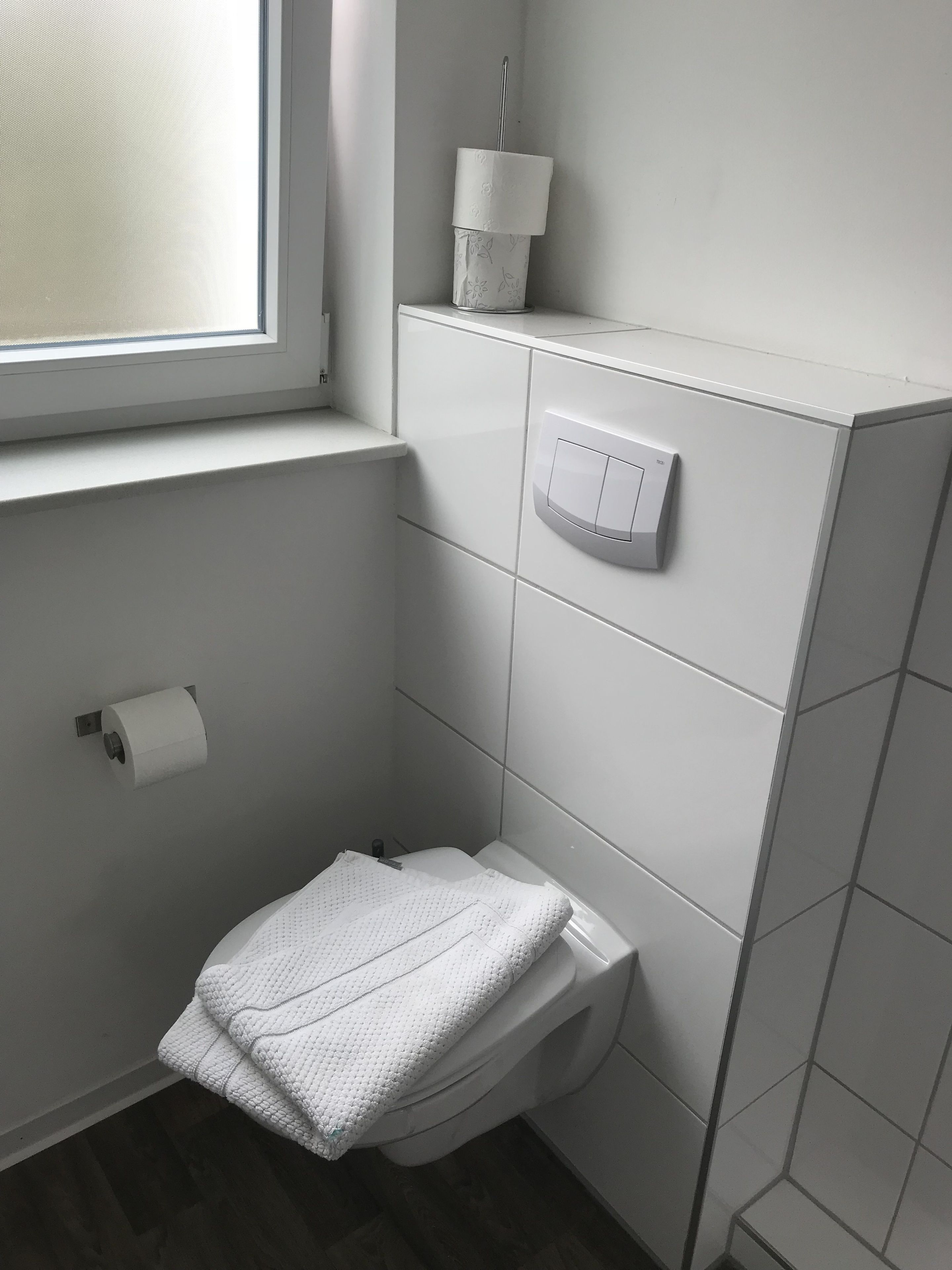 Casa de banho pequena e moderna, com sanita, secador de mãos e suporte para papel higiénico.