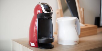Uma cafeteira vermelha e preta e uma chaleira elétrica branca sobre uma superfície de madeira.