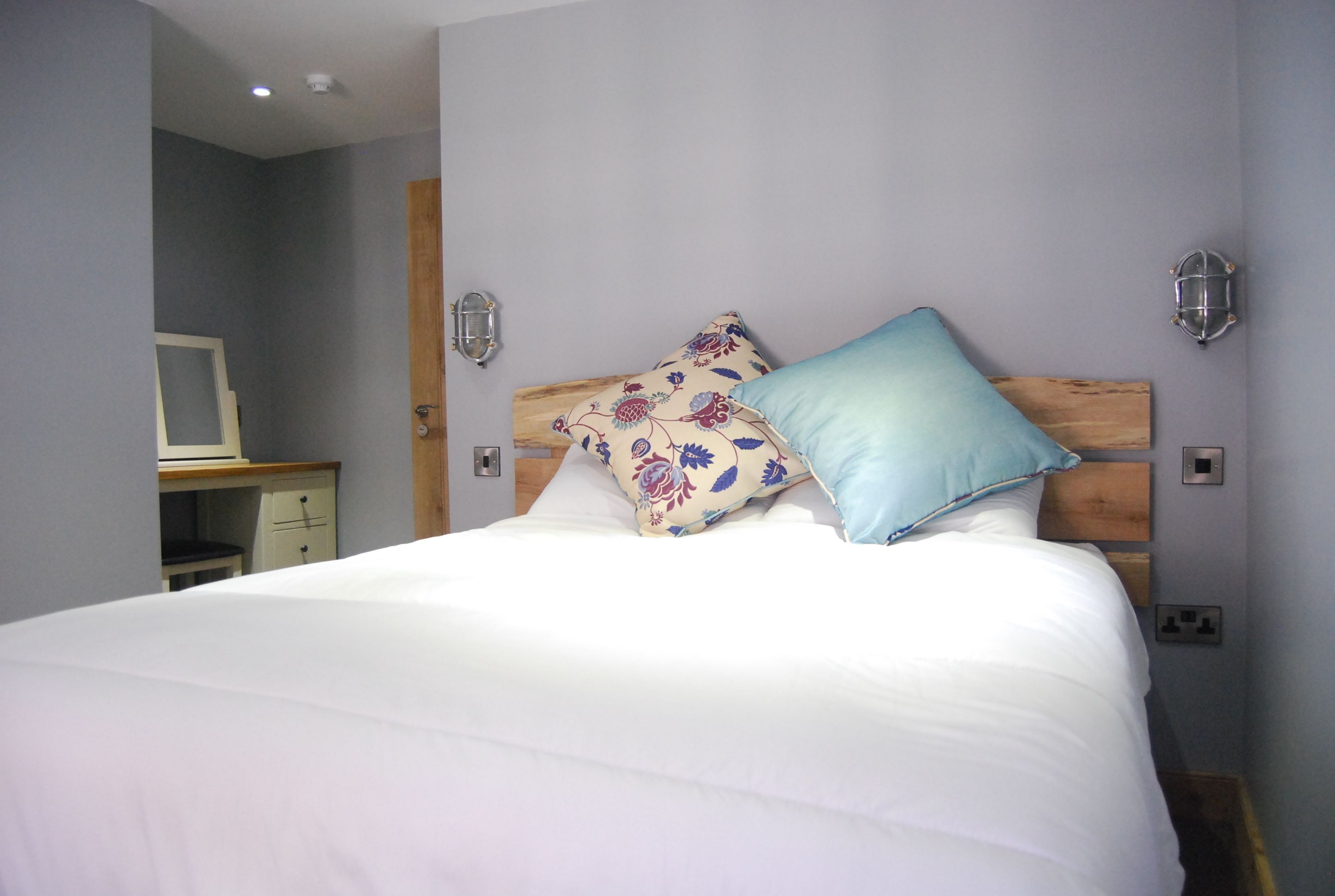 Quarto com cama, duas luminárias fixadas na parede e cabeceira de madeira.