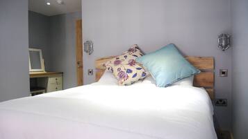 Quarto com cama, duas luminárias fixadas na parede e cabeceira de madeira.