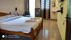 Quarto de hotel com cama, escrivaninha, cadeira, ar condicionado, espelho e pia.