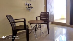 Quarto com televisão de tela plana na parede, uma mesinha com duas cadeiras e uma porta que dá para um espaço bem iluminado.