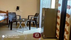 Quarto compacto com cama, uma mesinha, duas cadeiras, um refrigerador e um telefone na parede.