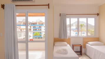 Quarto de hotel com duas camas, uma janela com cortinas, vista para edifícios e um aparelho de ar condicionado.