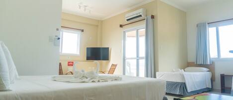 Quarto de hotel com duas camas, televisão, janela com cortinas e ar condicionado.