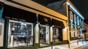 Um restaurante com fachada moderna, grandes janelas de vidro e rua de paralelepípedos.