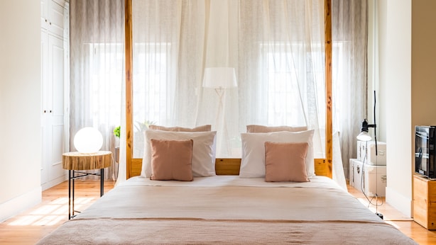 Quarto com uma cama grande, mesa de cabeceira com abajur e cortinas.