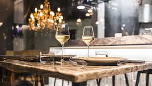 Mesa de jantar com duas taças de vinho e um copo de água, num restaurante com um candelabro ao fundo.
