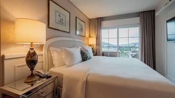 Quarto de hotel com cama grande, luminárias de cabeceira, telefone, mesinha de vidro e obras de arte emolduradas na parede.