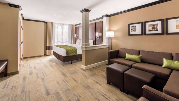 Quarto de hotel com cama, sofá, escrivaninha e quadros na parede.