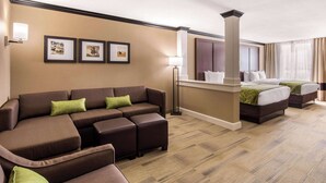 Quarto de hotel com sofá, banquinho, duas camas, escrivaninha e quadros na parede.