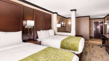 Quarto de hotel com duas camas, uma escrivaninha, uma cadeira e um espelho.