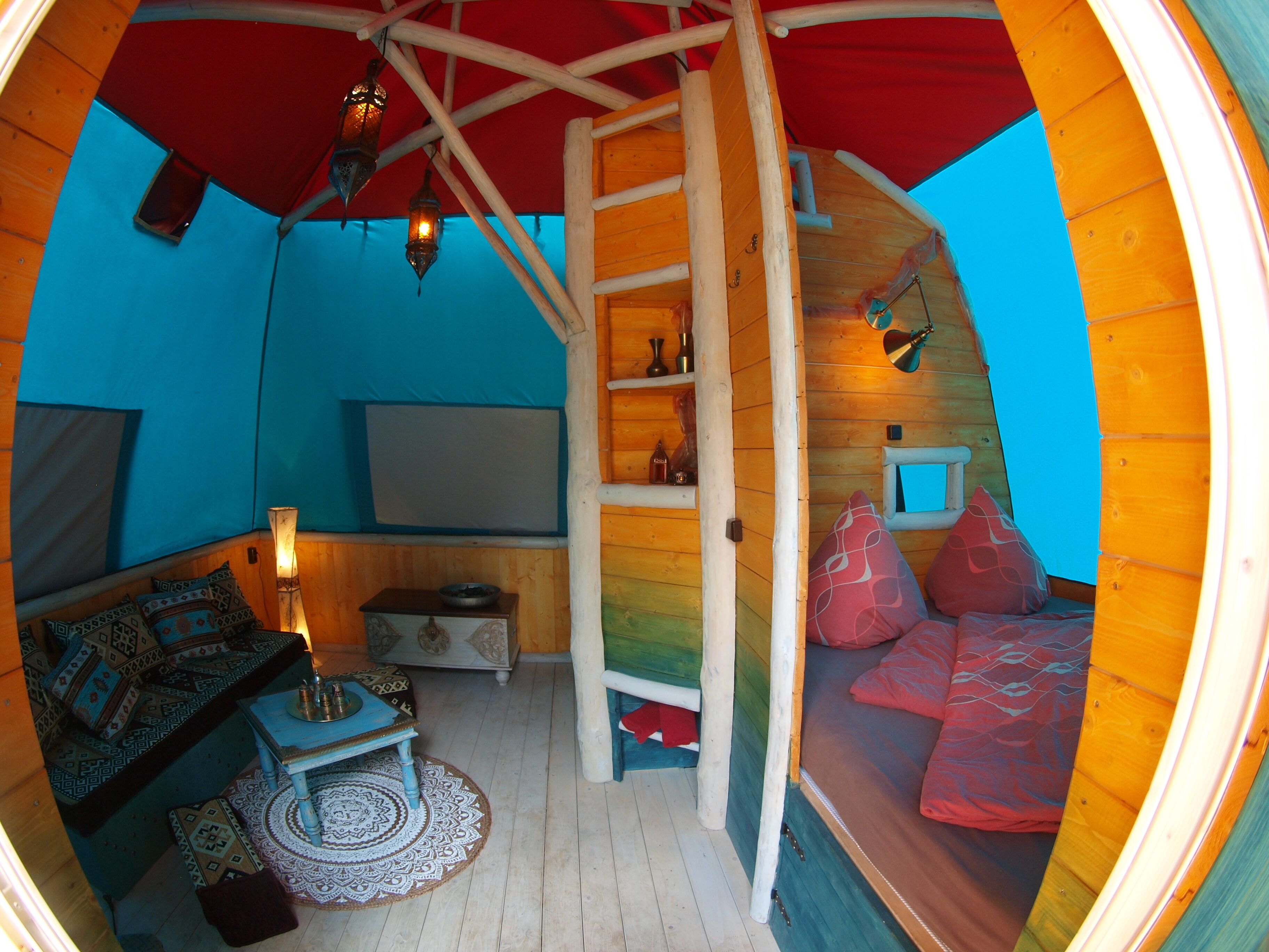 Um quarto aconchegante e circular, com uma escada de madeira, uma mesinha com abajur e um sofá com almofadas estampadas.