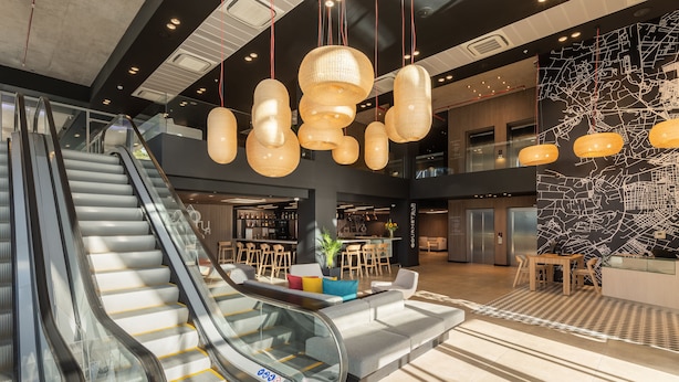 Espaço interior com escada rolante, área de estar e luminárias pendentes.