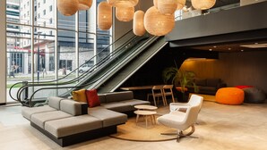 Um lobby moderno com uma ampla área de estar, uma escada rolante e grandes janelas com vista para a cidade.