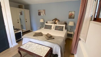 Quarto com cama, mesas de cabeceira, guarda-roupa e uma pequena mesa com toalhas.