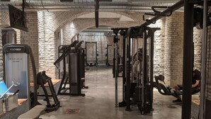 Uma academia com paredes de tijolo, diversos equipamentos de exercício e uma máquina de desenvolvimento de pernas.