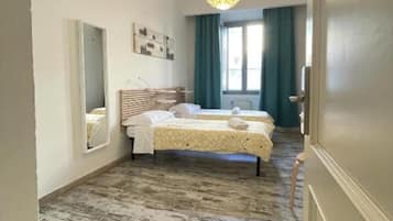 Quarto de hotel com cama, espelho, janela com cortinas e luminária pendente.