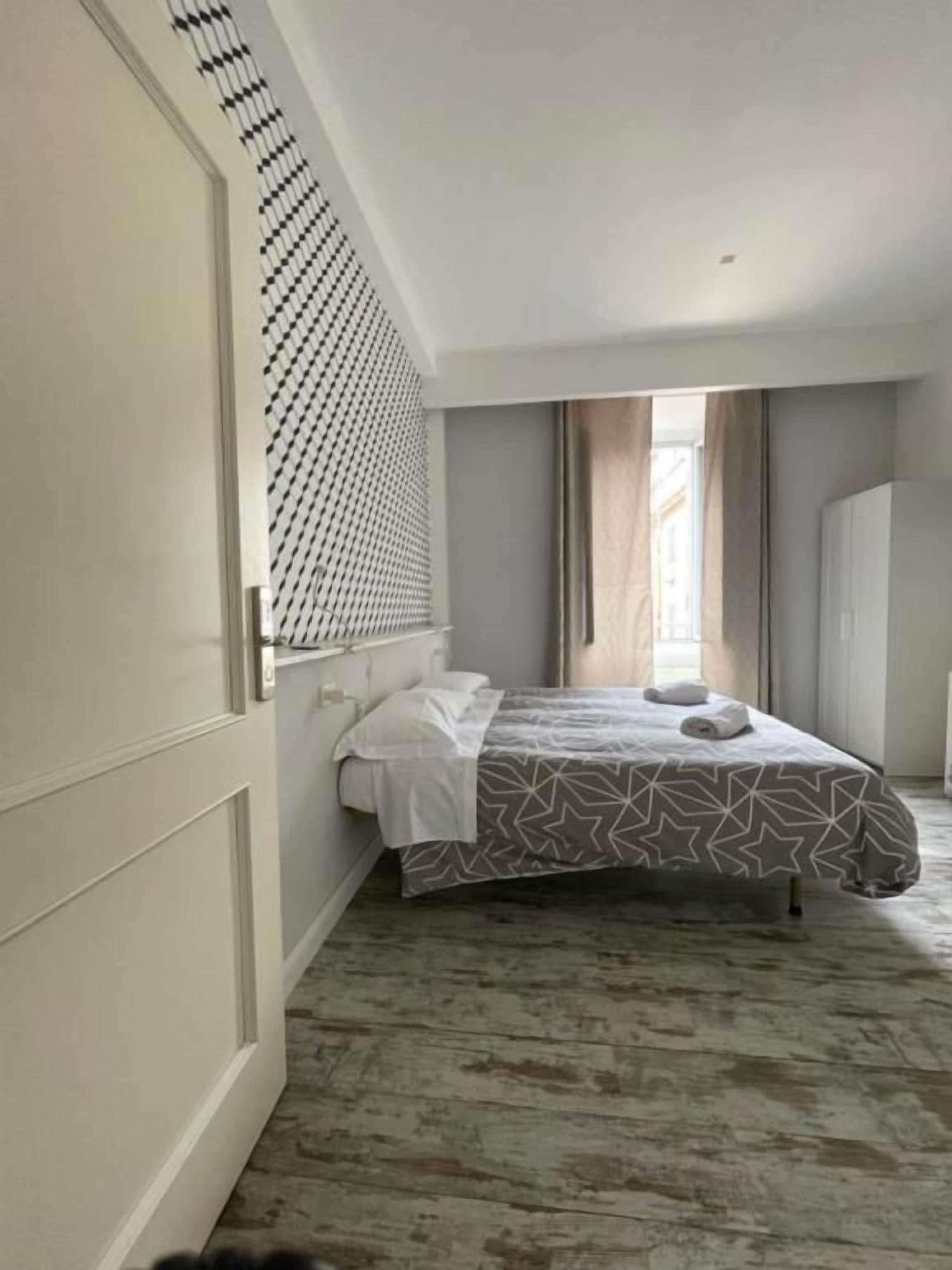 Quarto com cama, janela com cortinas, guarda-roupa e colcha estampada.