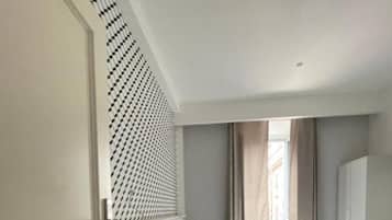 Quarto com cama, janela com cortinas, guarda-roupa e colcha estampada.
