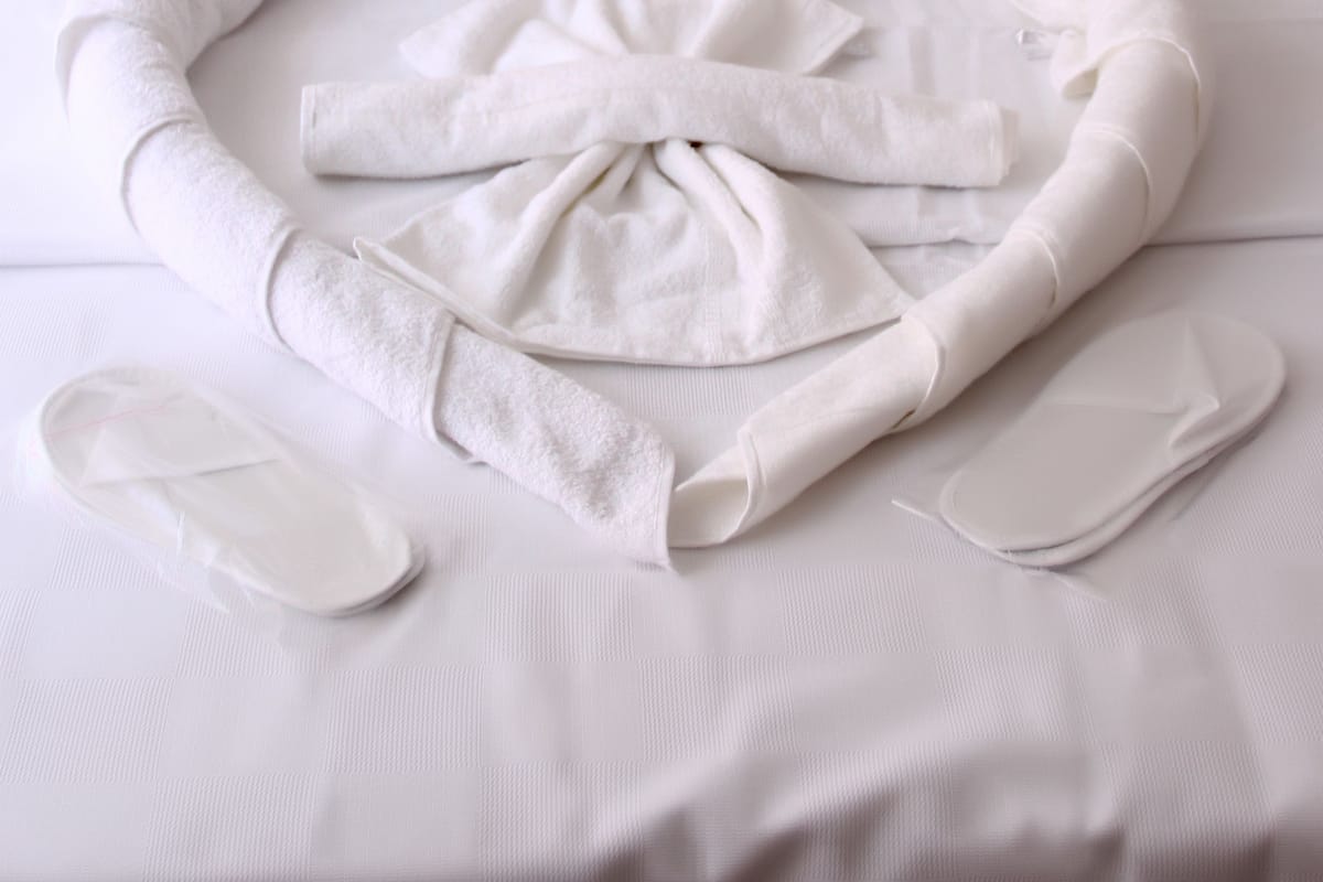 Uma cama com arranjo de toalhas em formato de coração e chinelos.